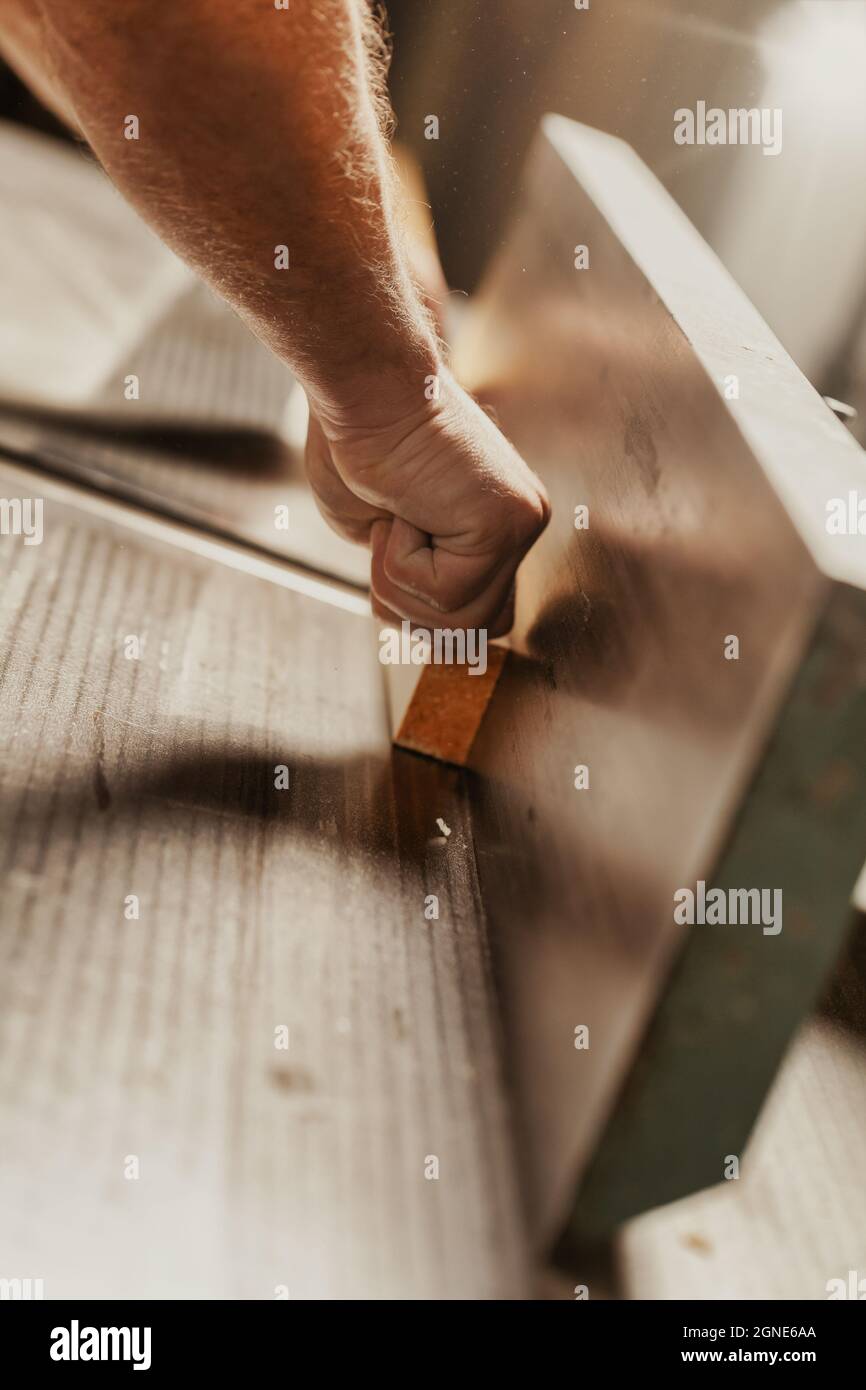Carpenter guiding a block of wood across a workbench and power tool in ...