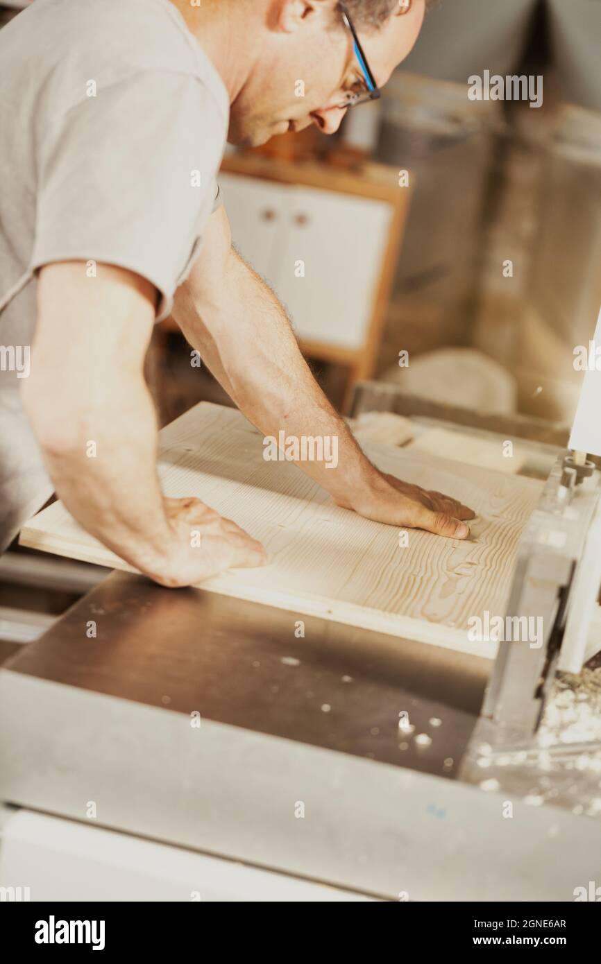 Carpenter guiding a block of wood over a workbench past a plane or saw ...