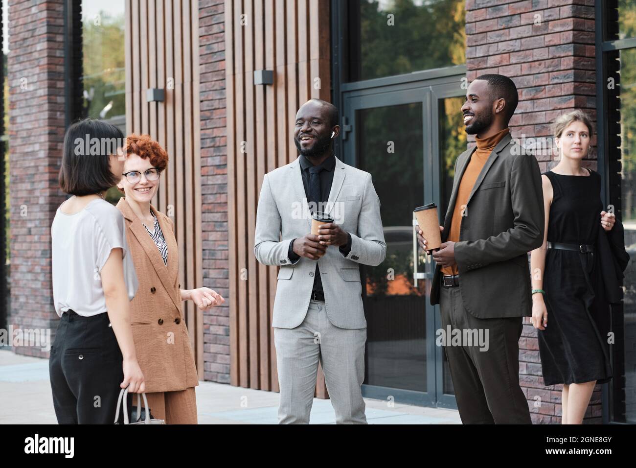 Medium long shot of multi-ethnic co-workers standing outdoors drinking ...