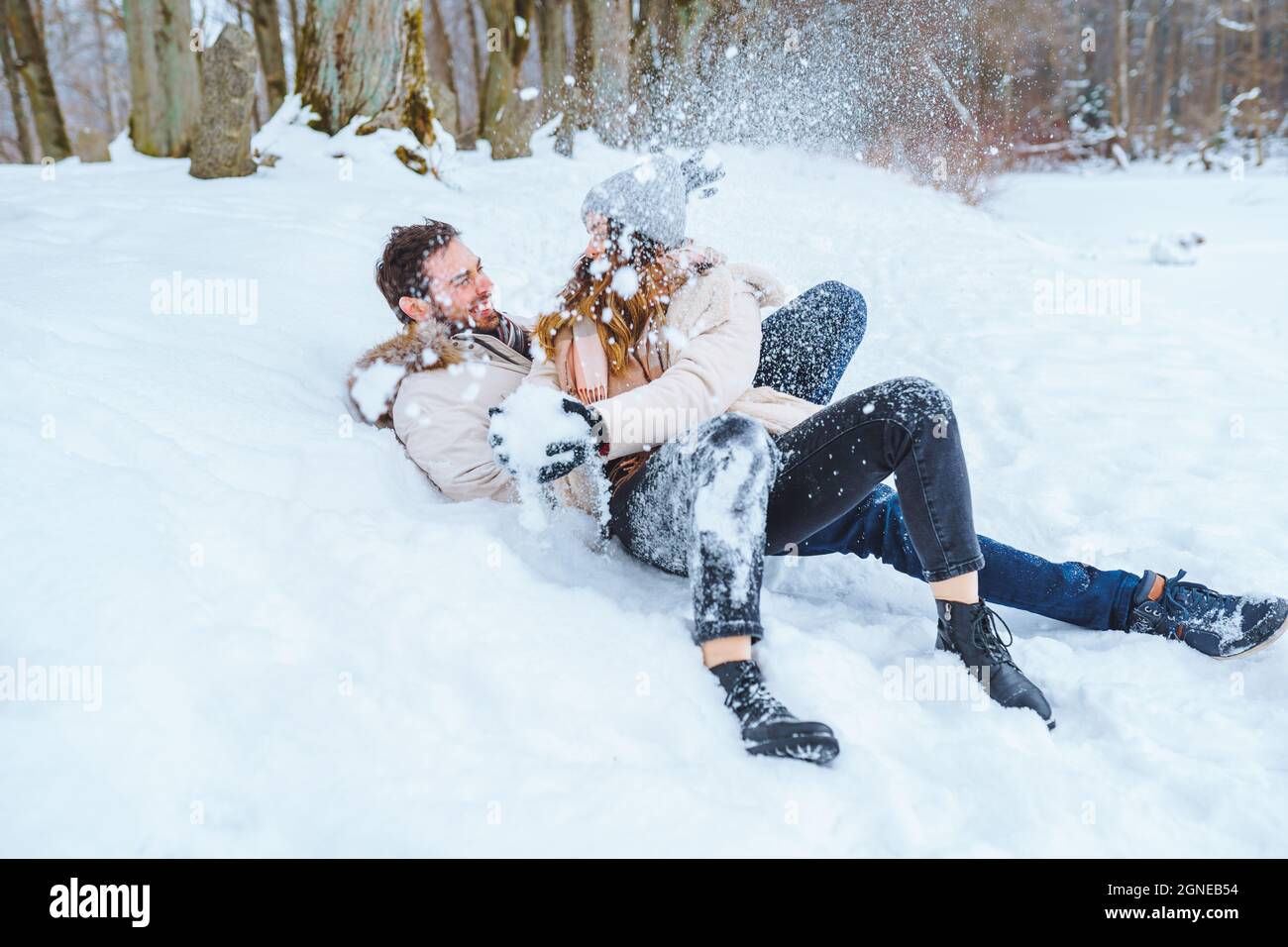 Young happy couple lie in the snow, throw snow and play in the winter ...