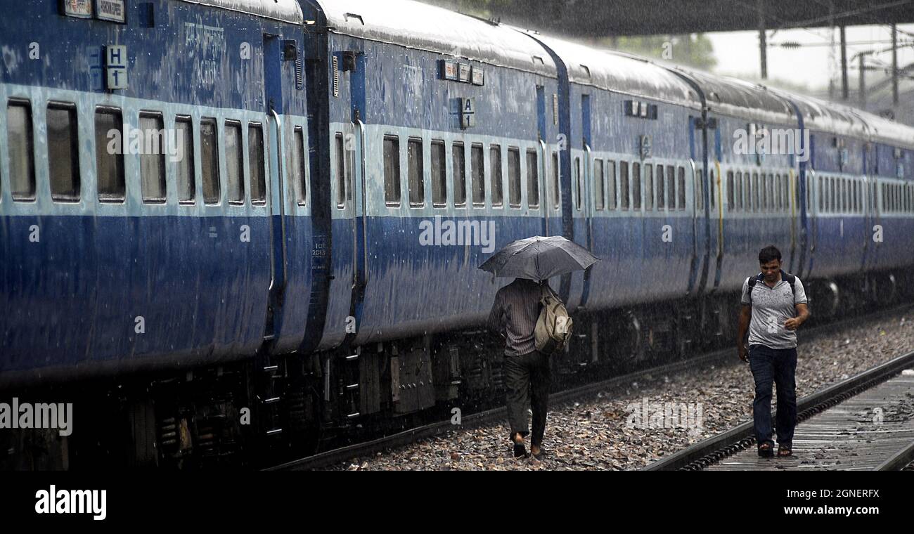 Indian Commuters walk on railway tracks during the rain as a train ...