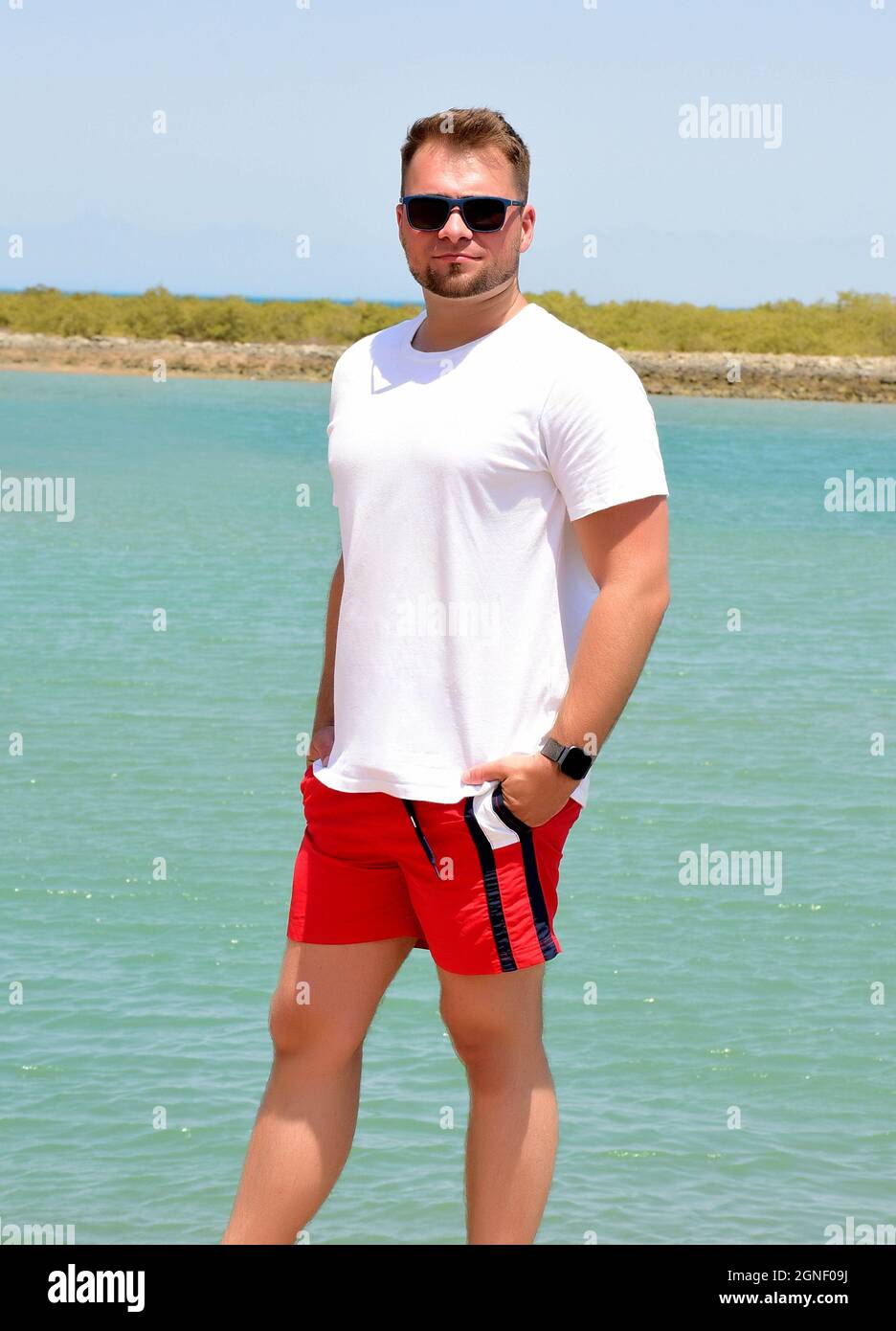 young man poses in front of the sea, with a small island in the ...