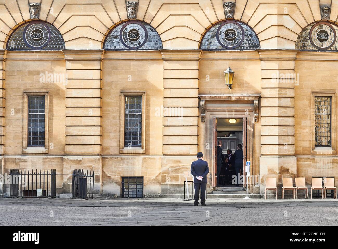 A lone security guard with bowler hat waits in the courtyard outside ...