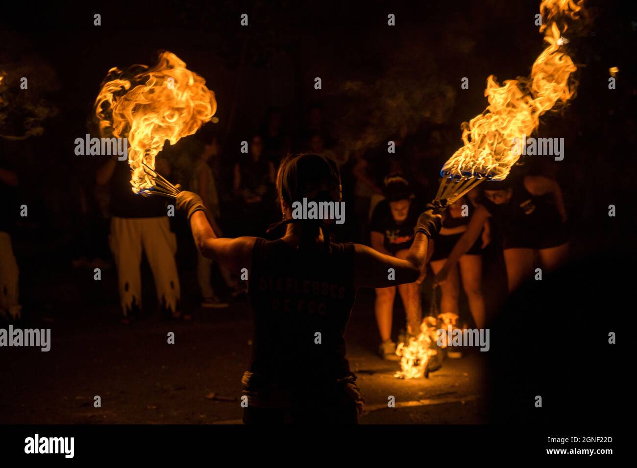 Fire dancer holding flaming fans from behind illuminating dark scene ...