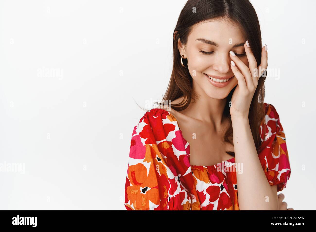 Attractive brunette girl giggle, gazing down and touching her face ...