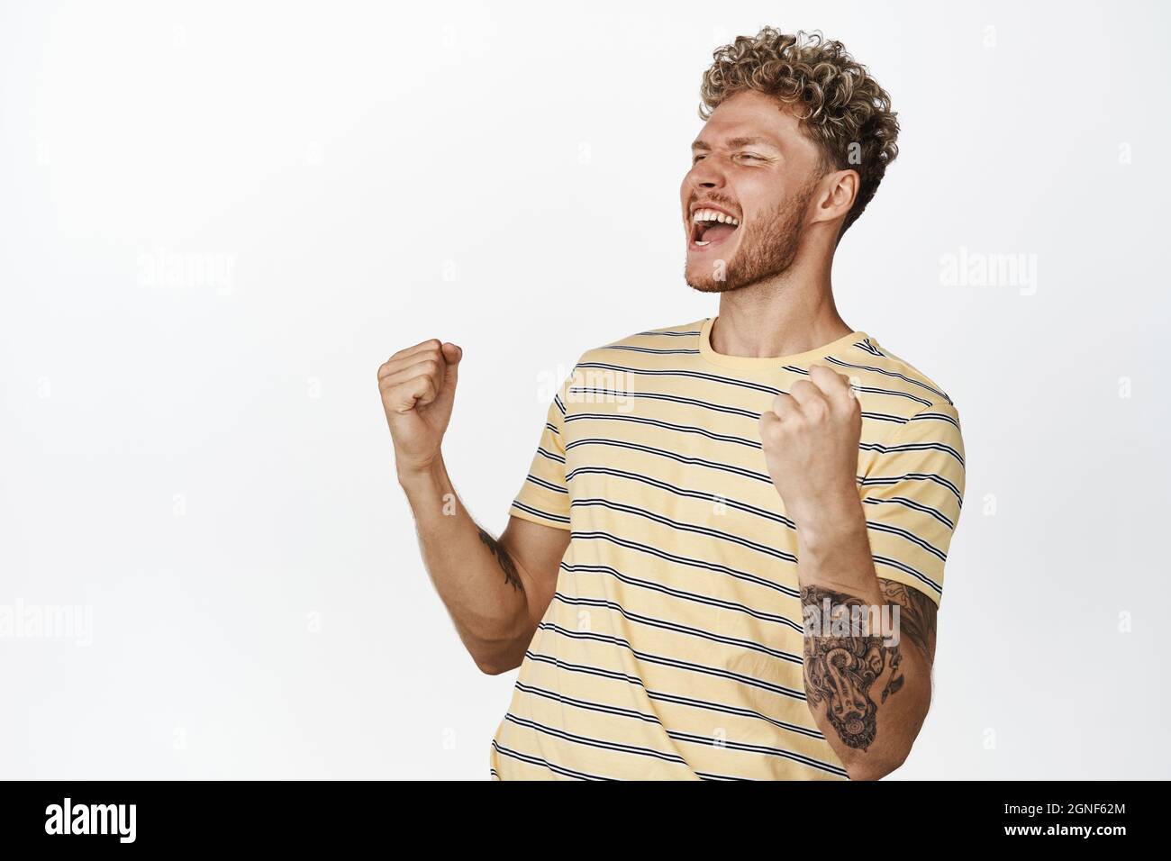 Happy blond guy celebrating success, making fist pump, shouting yes ...