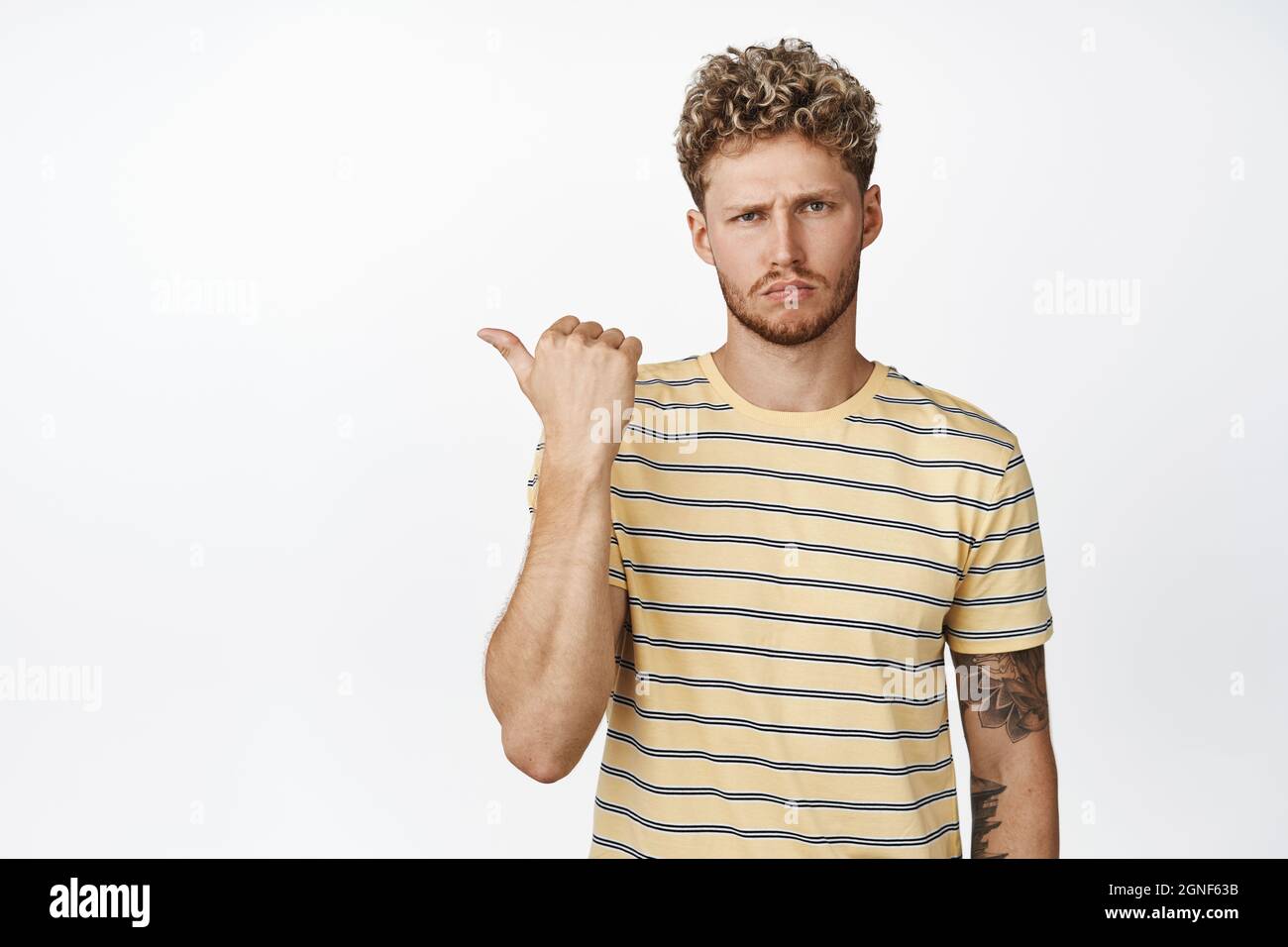 Upset young blond guy pointing finger left, looking disappointed and ...