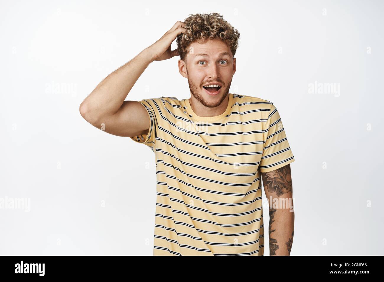 Surprised handsome guy smiling, awkwardly scratching his head, looking ...