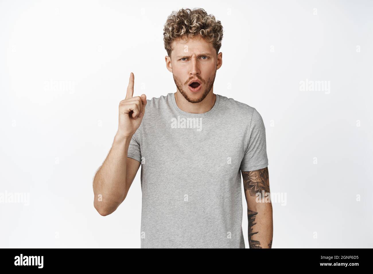 Confused blond man pointing finger up, staring questioned at camera ...