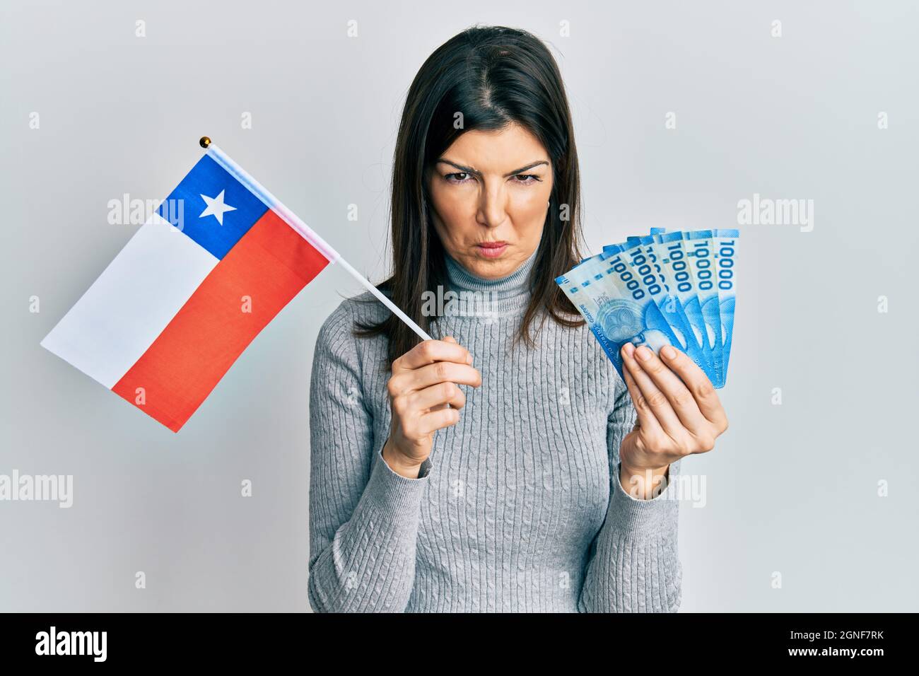 Young hispanic woman holding chile flag and chilean pesos banknotes ...
