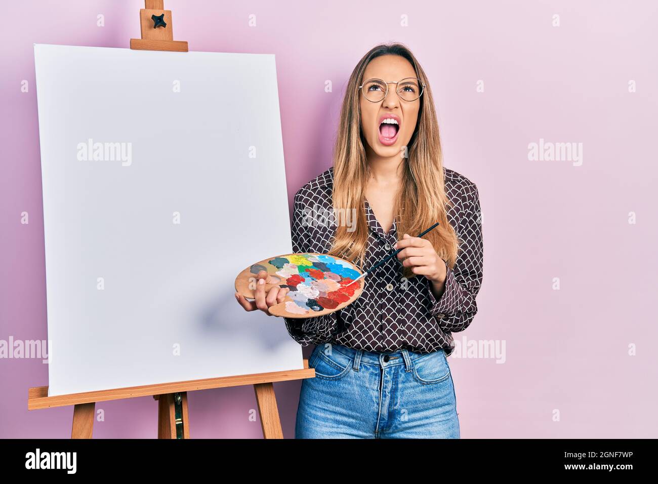Beautiful hispanic woman standing drawing with palette by painter easel ...