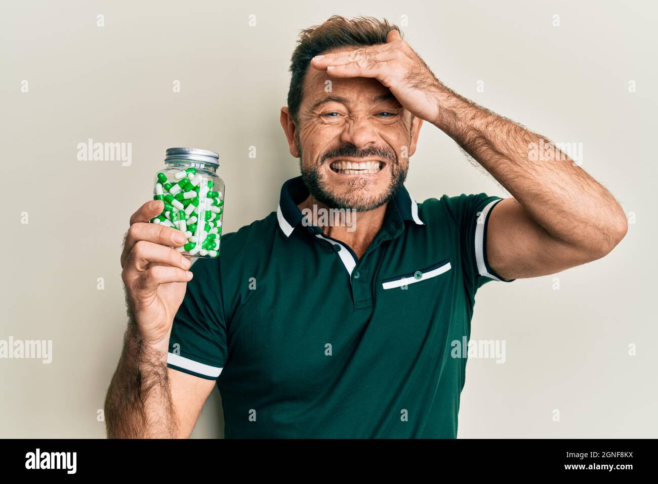 Middle age man holding pills stressed and frustrated with hand on head ...