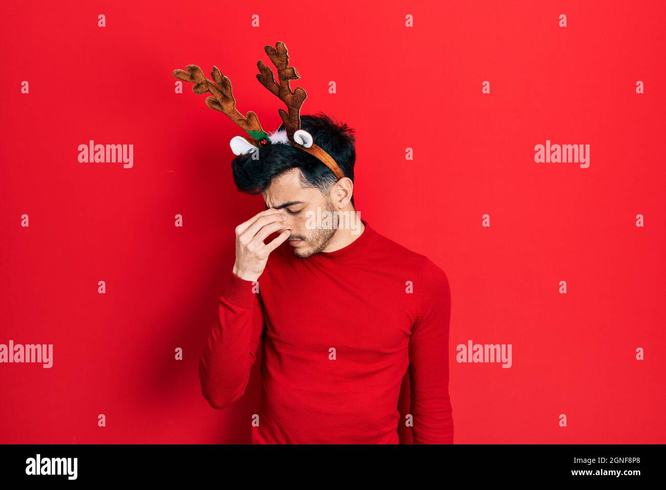 Young hispanic man wearing cute christmas reindeer horns tired rubbing ...
