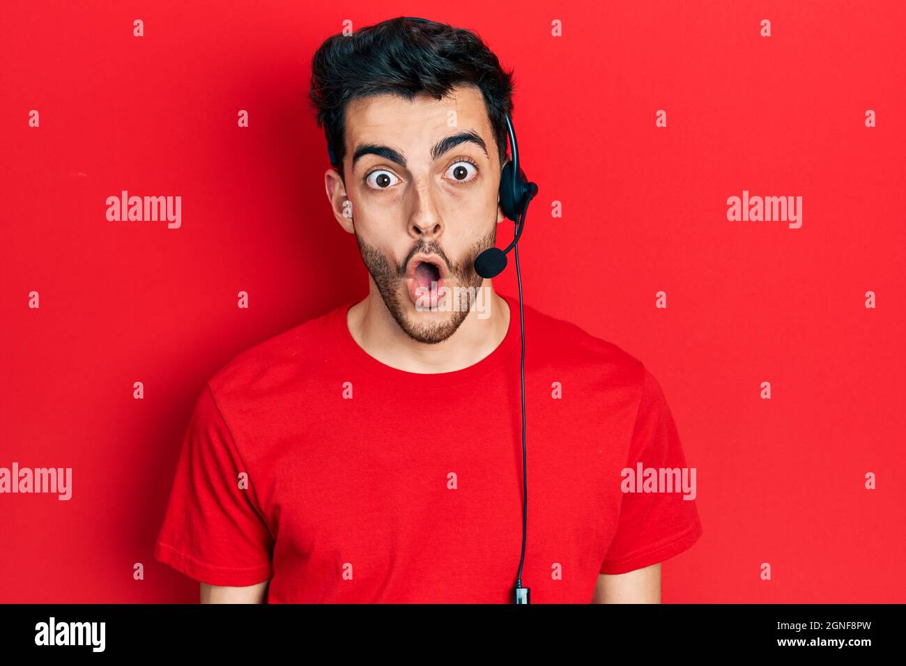 Young hispanic man wearing call center agent headset scared and amazed ...