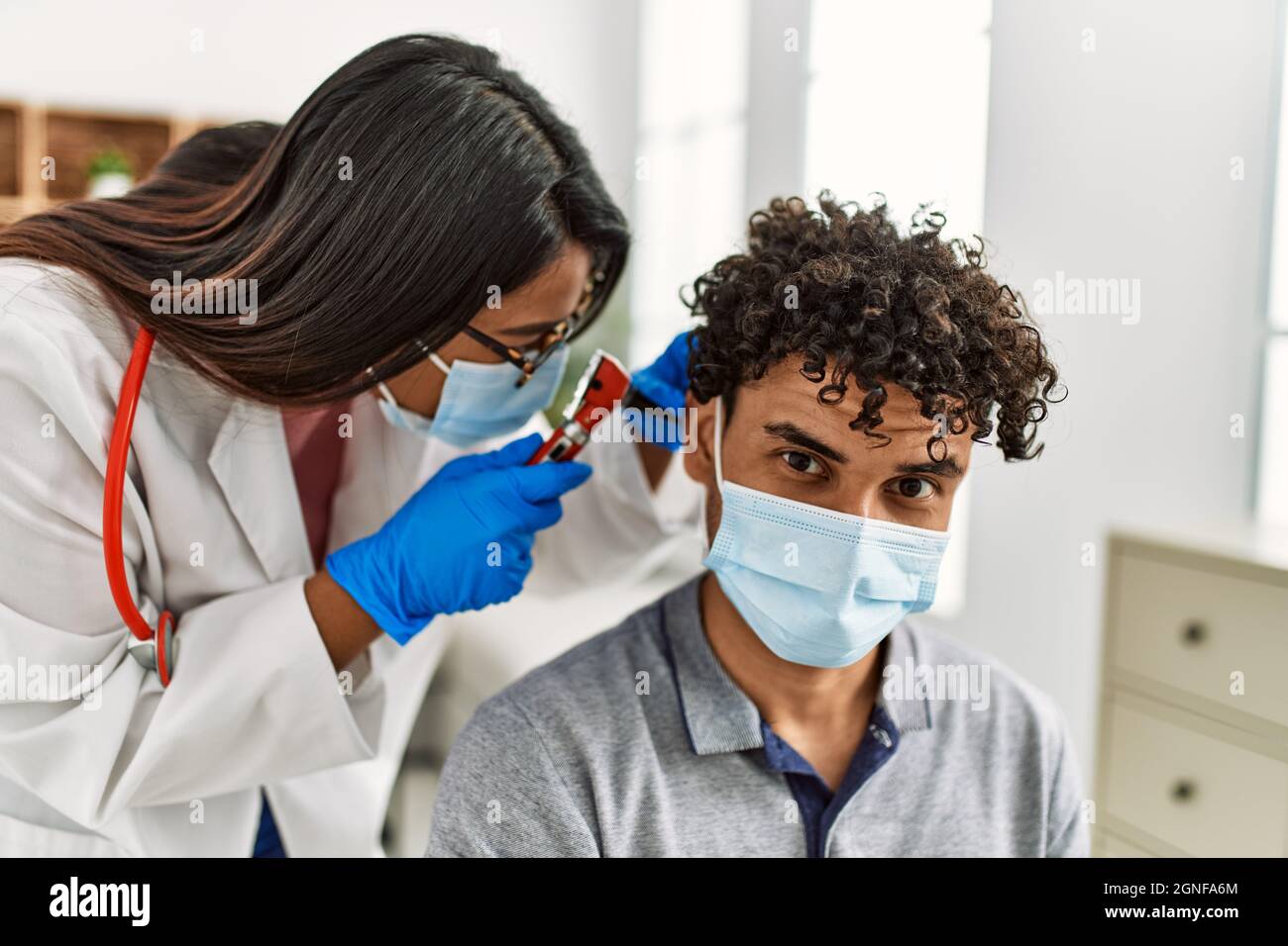 Young latin doctor woman auscultating the ear of man using otoscope at ...