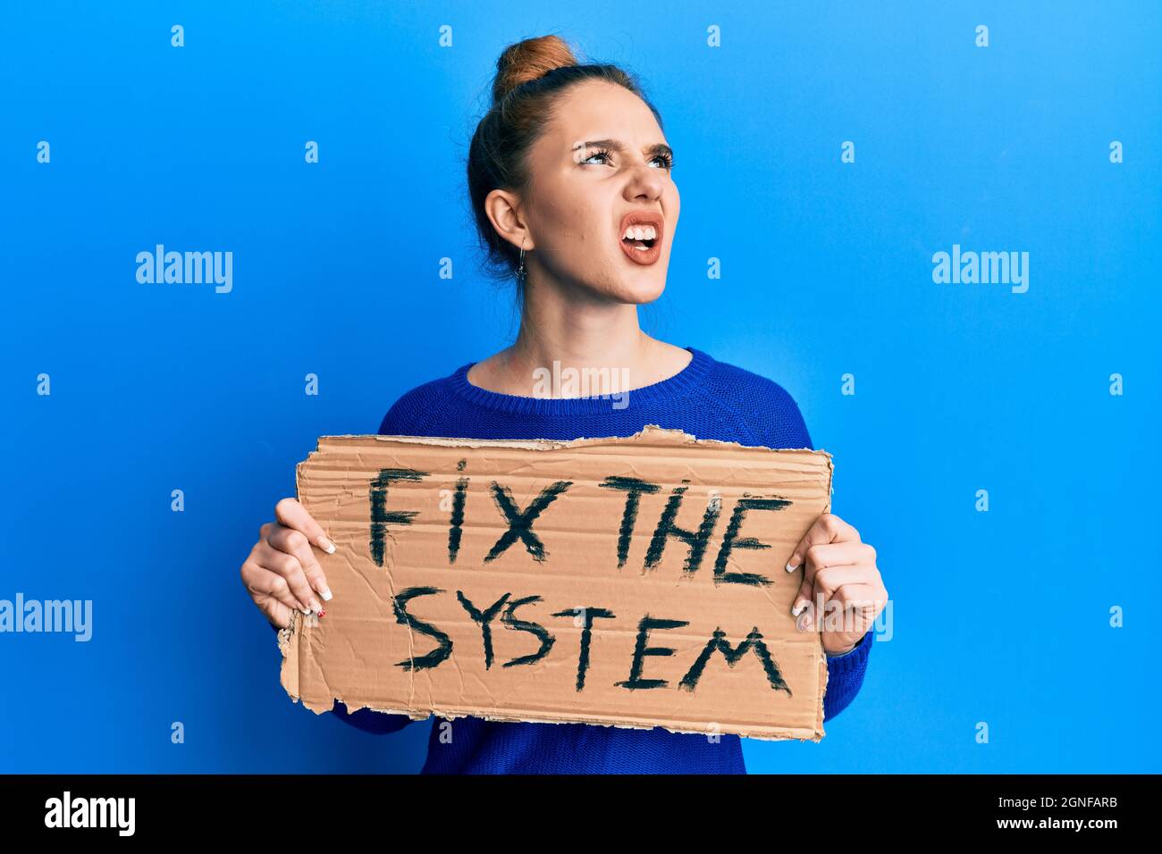 Young blonde woman holding fix the system banner cardboard angry and ...