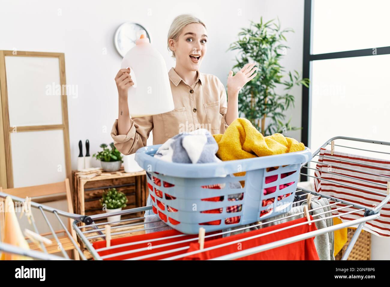 Young caucasian woman doing laundry holding detergent bottle celebrating achievement with happy ...