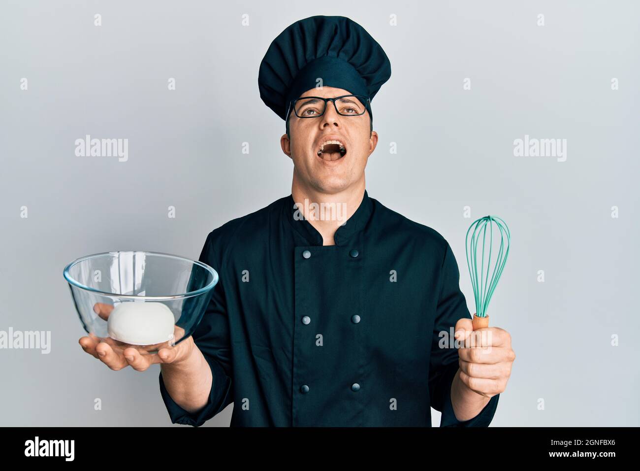 Handsome young man holding bread dough and blender angry and mad ...