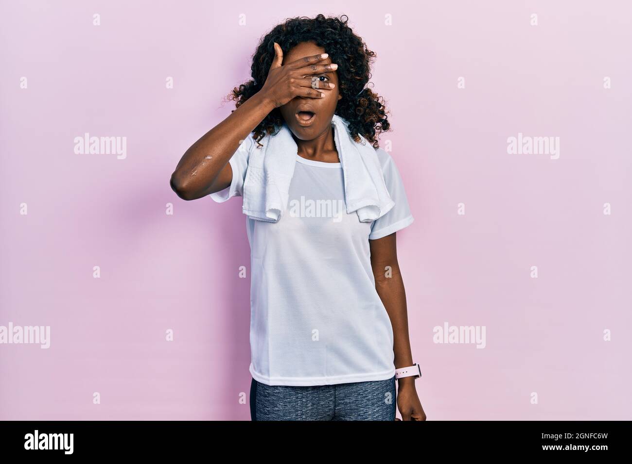 Young african american woman wearing sportswear and towel peeking in ...