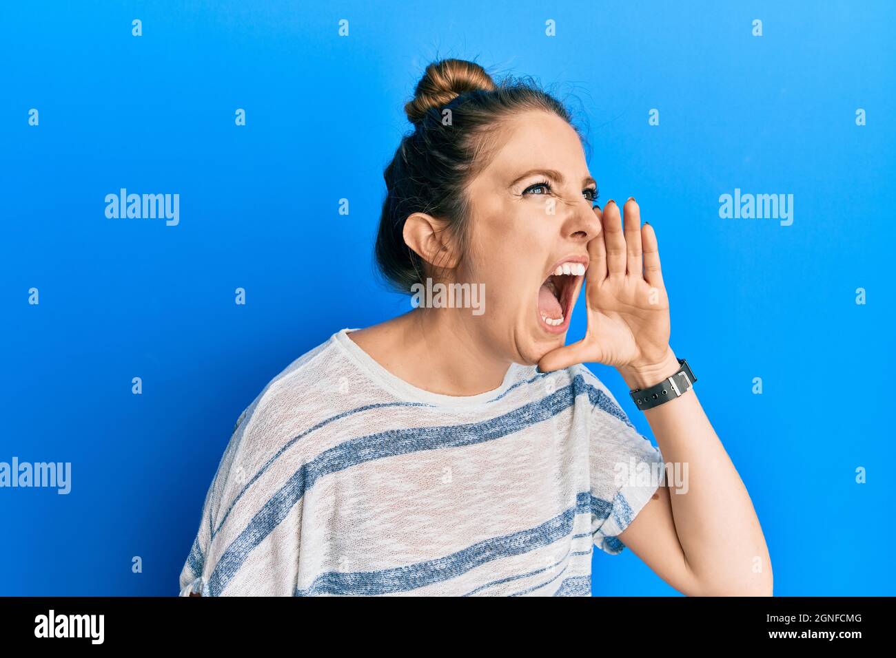 Young blonde woman wearing casual striped t shirt shouting and ...