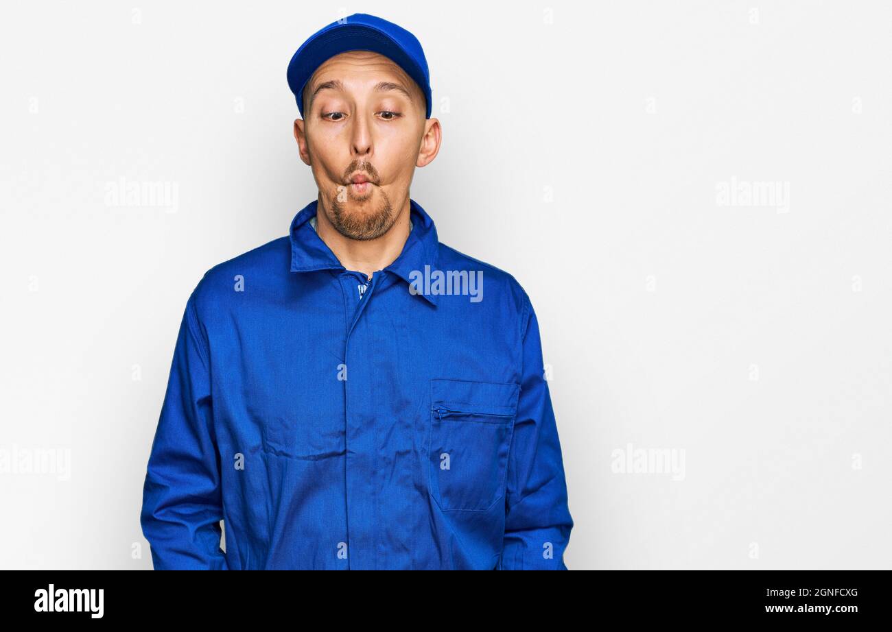 Bald man with beard wearing builder jumpsuit uniform making fish face ...