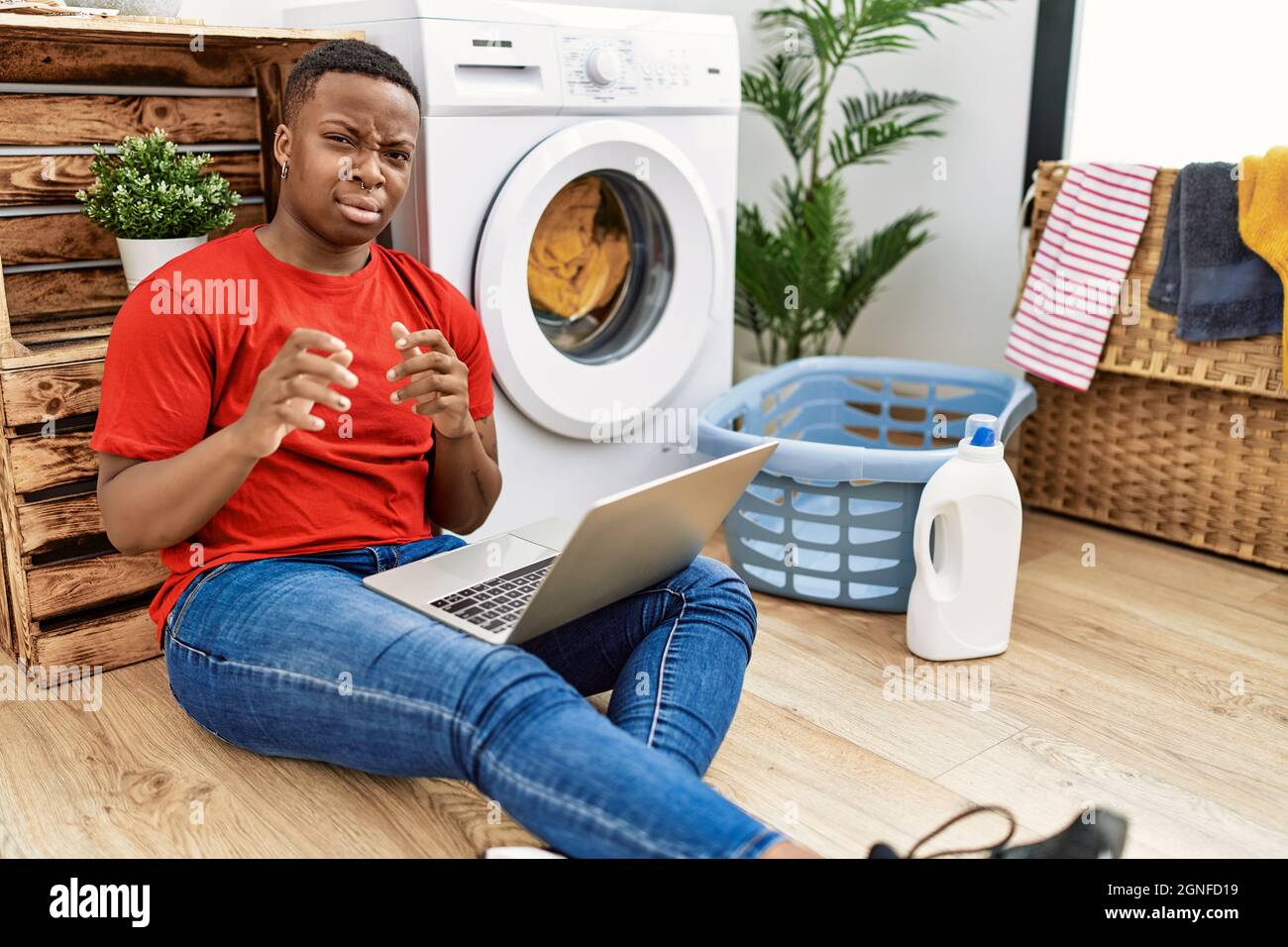 Young african man doing laundry and using computer disgusted expression ...