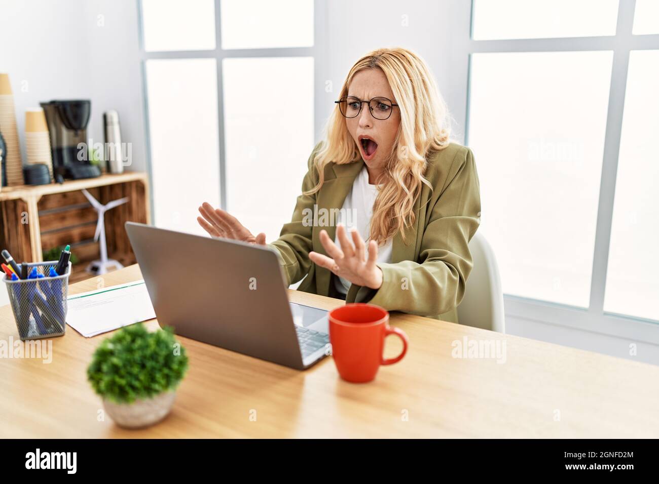 Beautiful blonde woman working at the office with laptop afraid and ...
