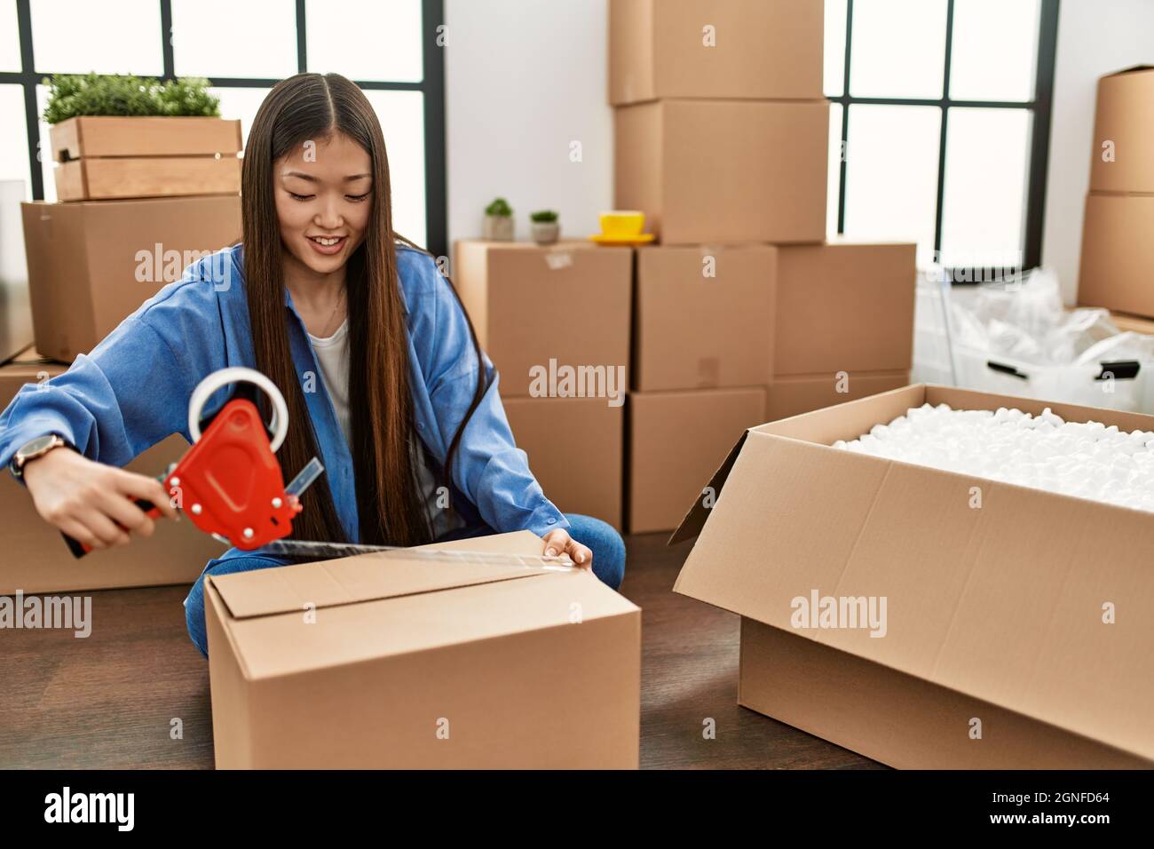 Young chinese girl smiling happy closing box using packing tape at new ...