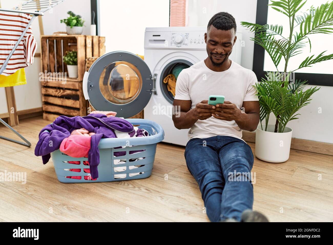 Young african man doing laundry using smartphone looking positive and ...