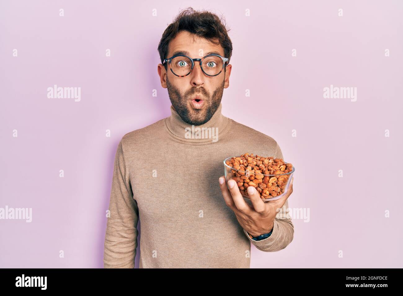 Handsome man with beard holding peanuts scared and amazed with open ...