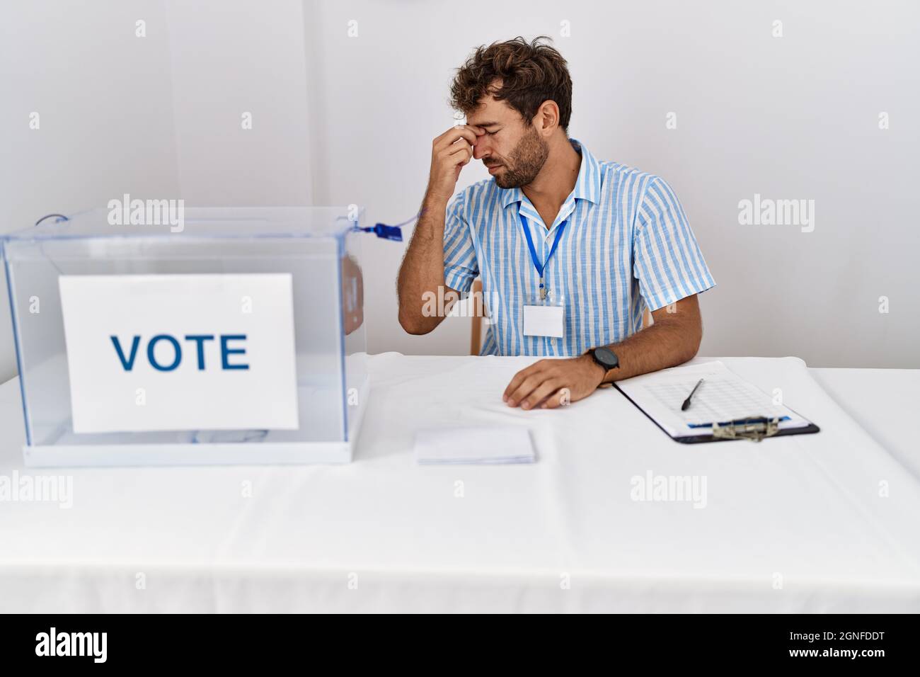 Young handsome man at political election sitting by ballot tired ...