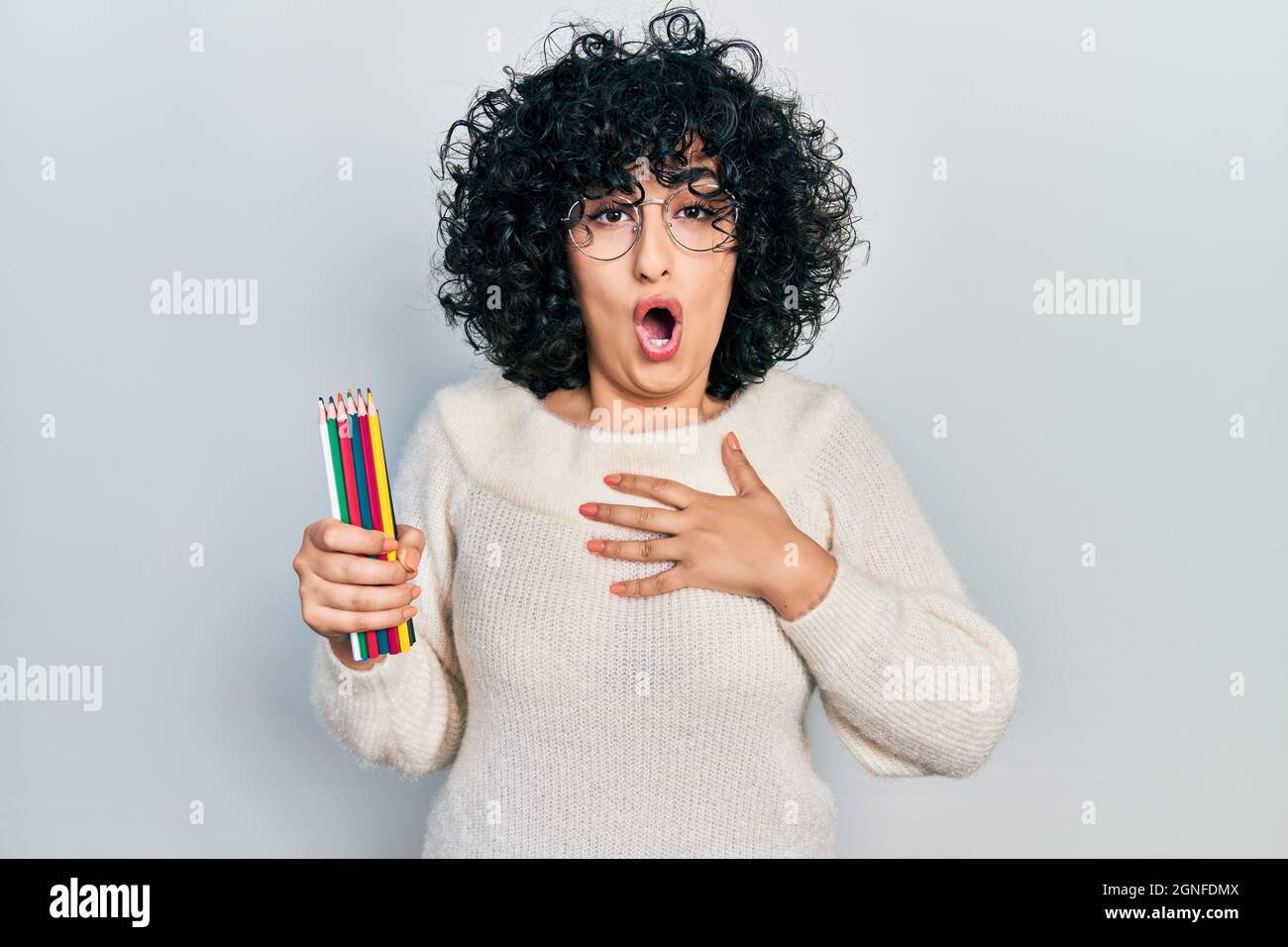 Young middle east woman holding colored pencils scared and amazed with ...
