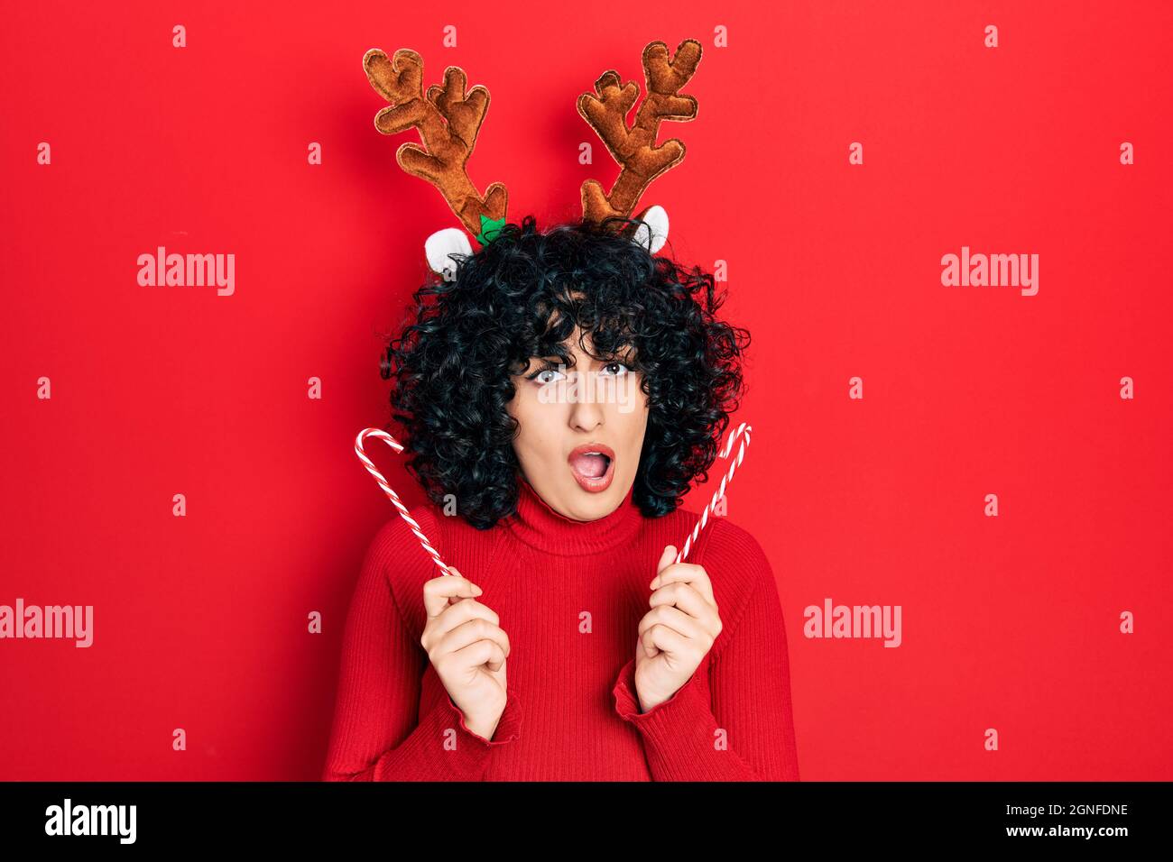 Young middle east woman wearing cute christmas reindeer horns in shock ...