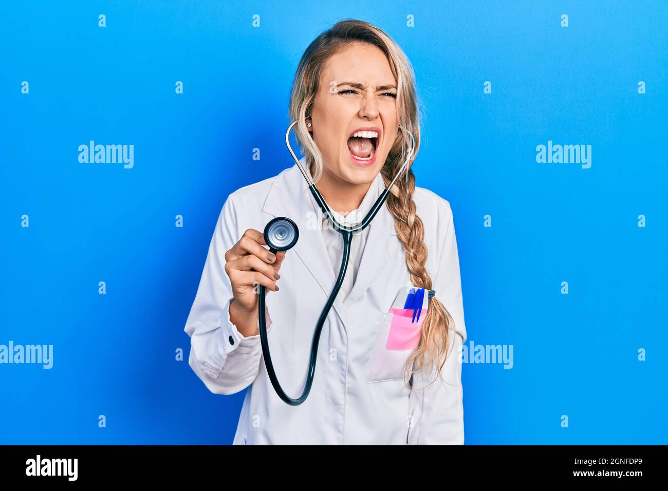 Beautiful young blonde doctor woman holding stethoscope angry and mad ...