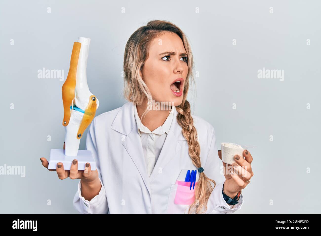 Beautiful young blonde doctor woman holding anatomical model of knee ...