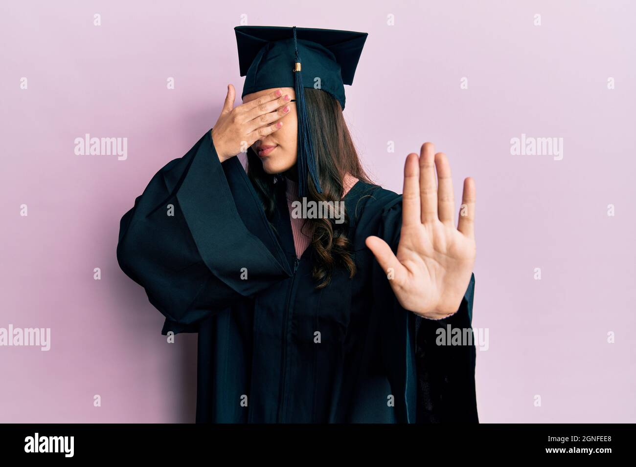 Young hispanic woman wearing graduation cap and ceremony robe covering ...