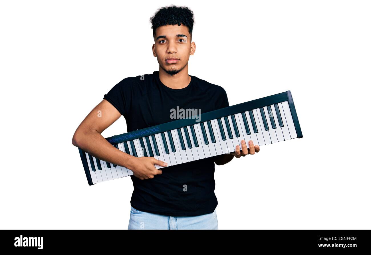 Young african american man holding piano keyboard relaxed with serious ...