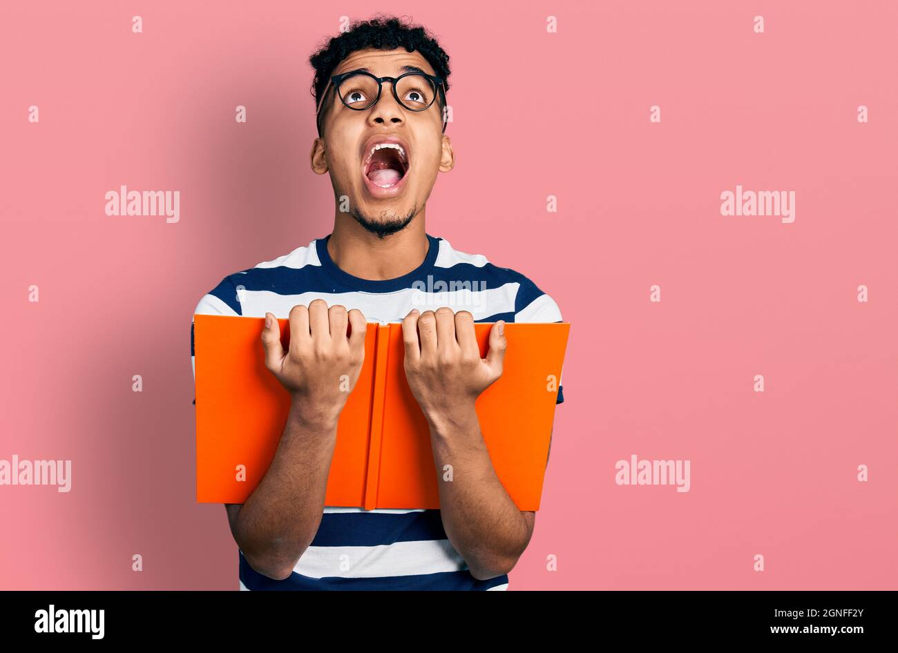 Young african american man reading a book with glasses angry and mad ...