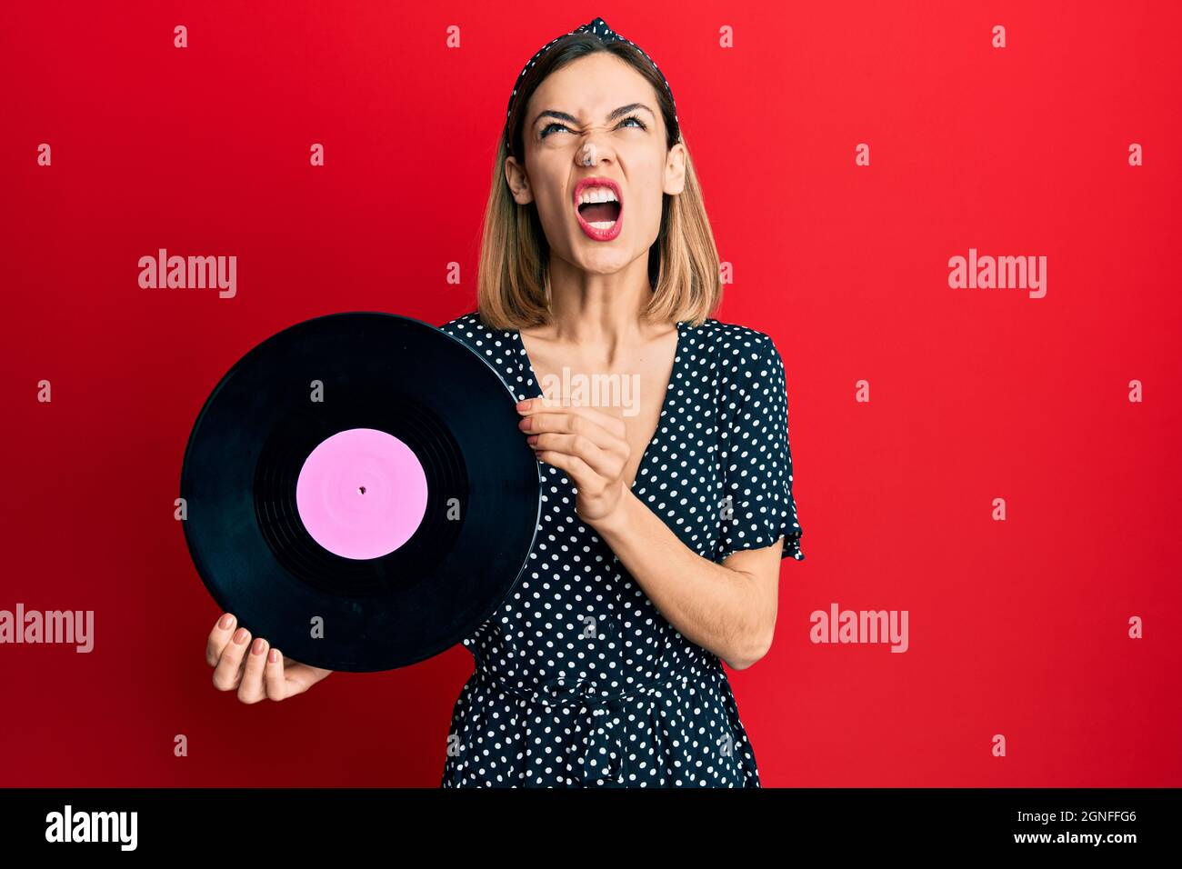 Young caucasian blonde woman holding vinyl disc angry and mad screaming ...
