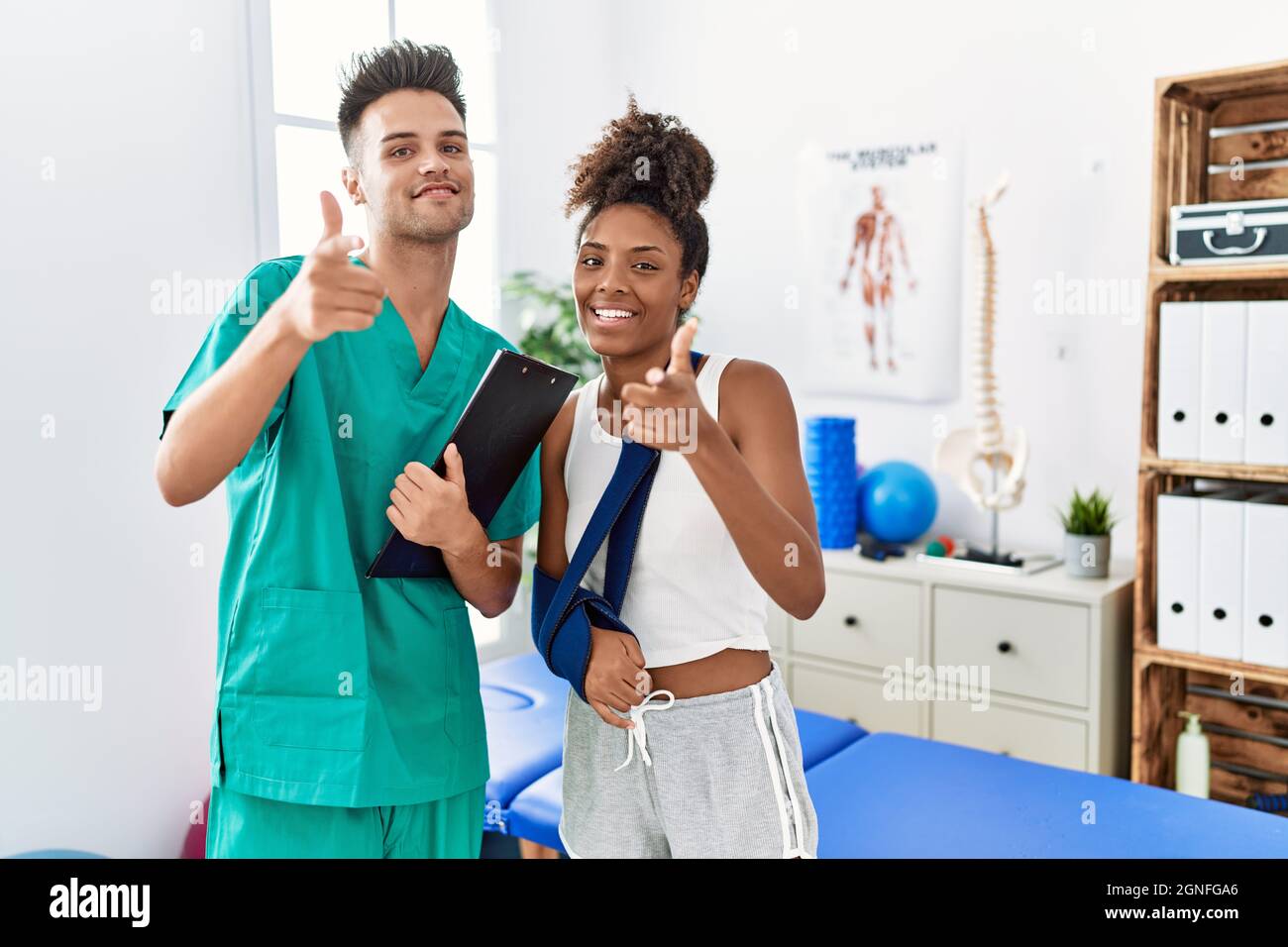 Physiotherapist working with patient wearing arm on sling at rehabilitation clinic pointing ...