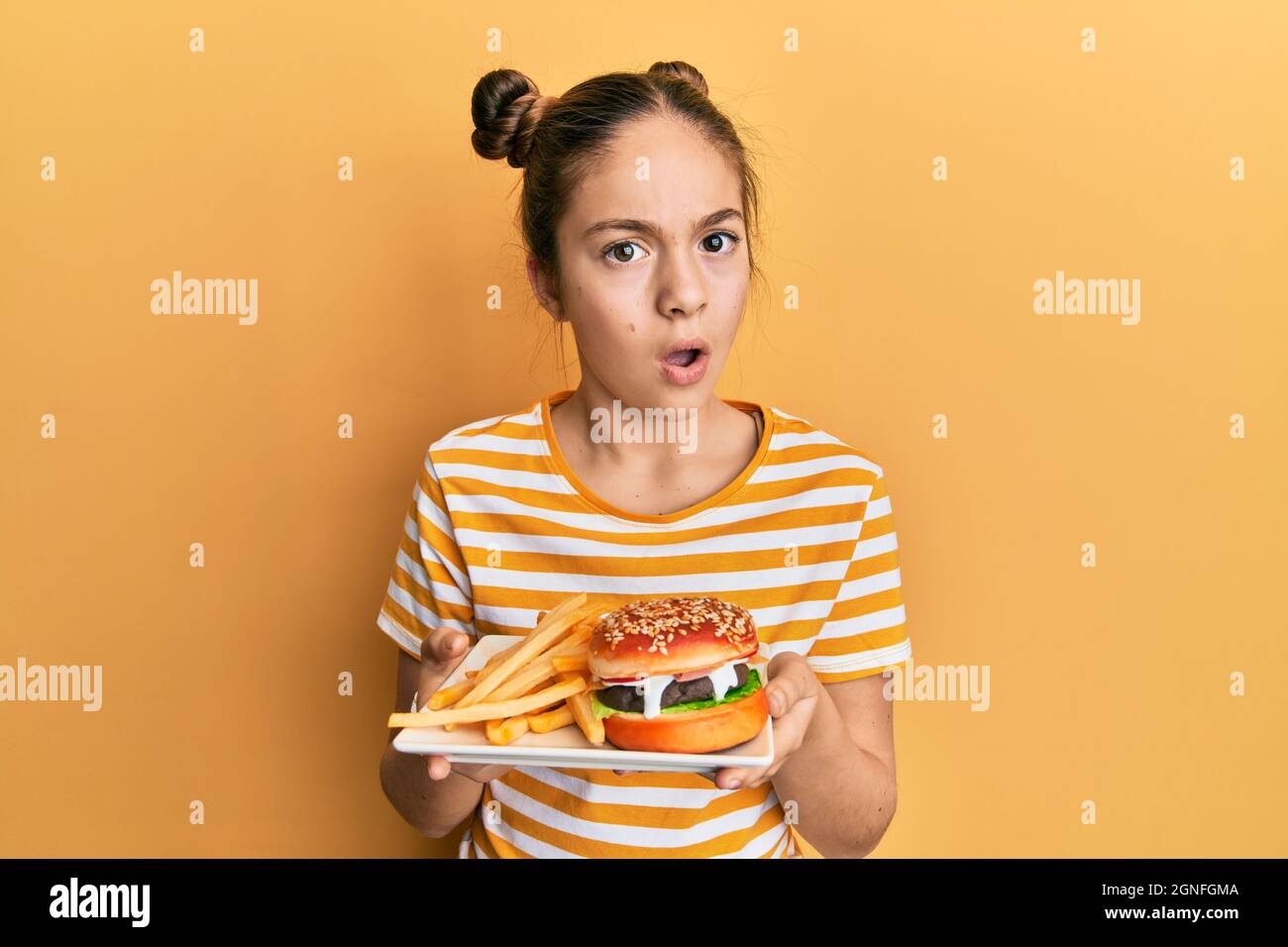 Beautiful brunette little girl eating a tasty classic burger with fries ...