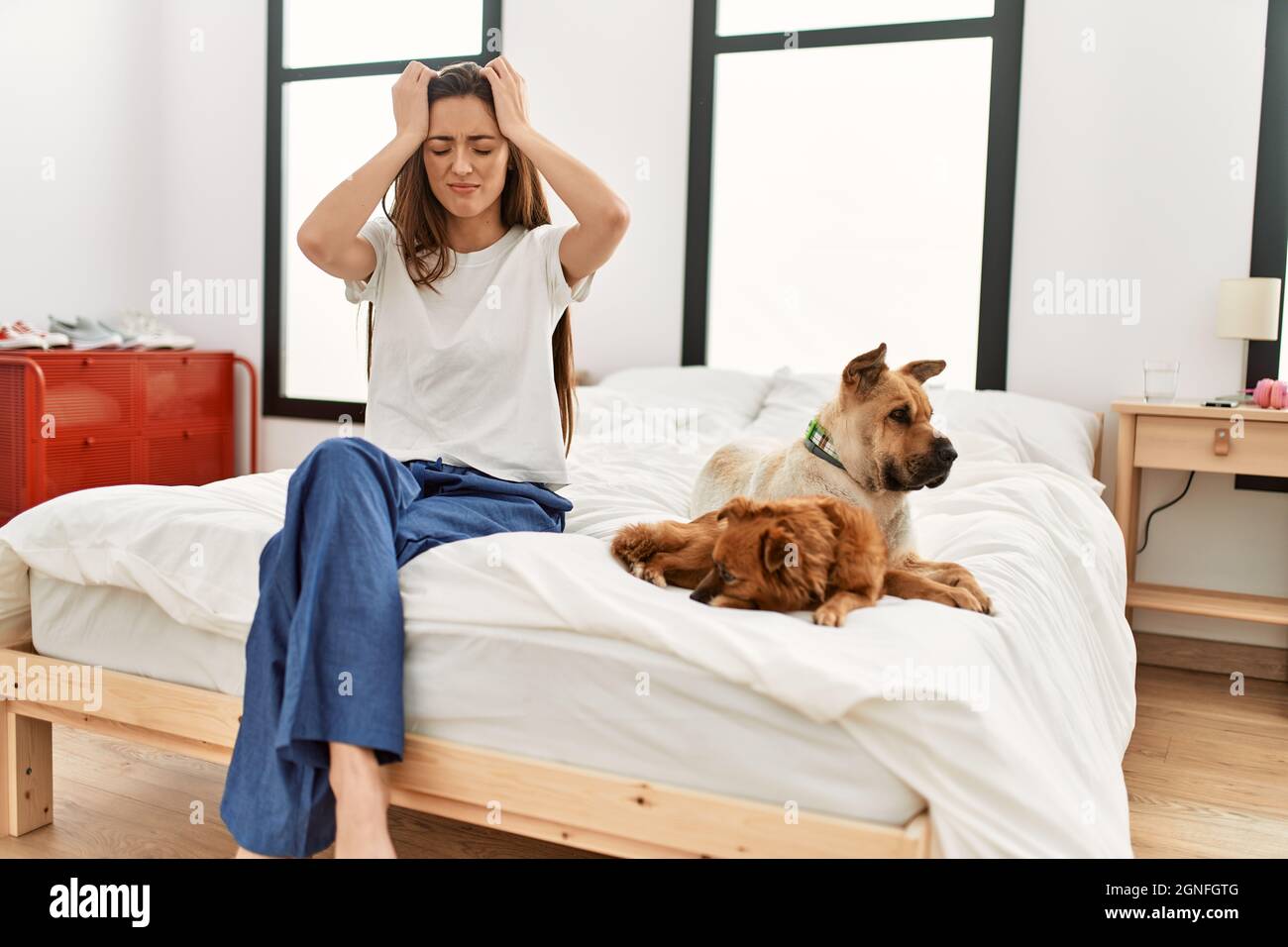 Young brunette woman sitting on the bed with two dogs suffering from ...