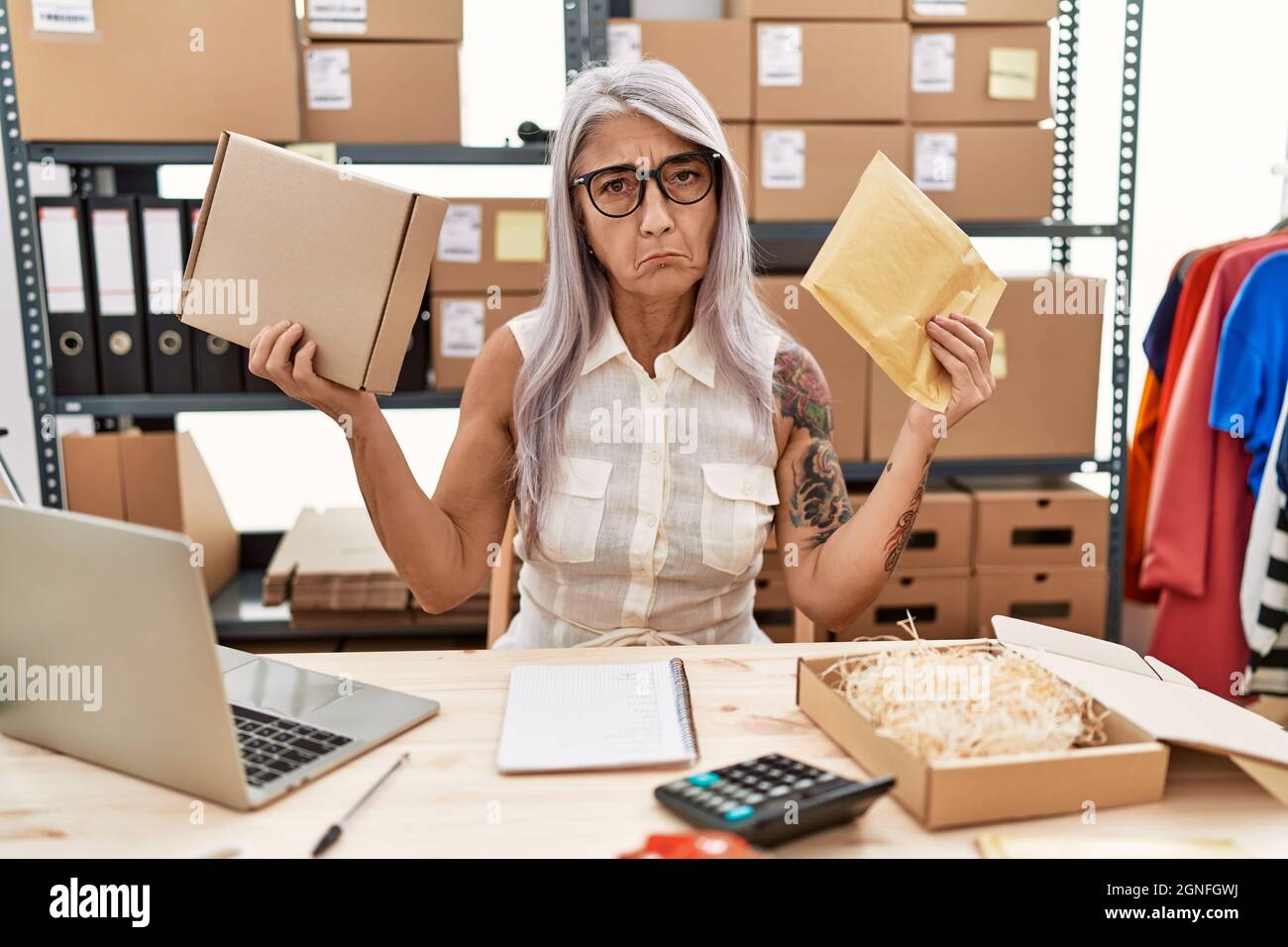 Middle age grey-haired woman holding package and envelope at warehouse ...