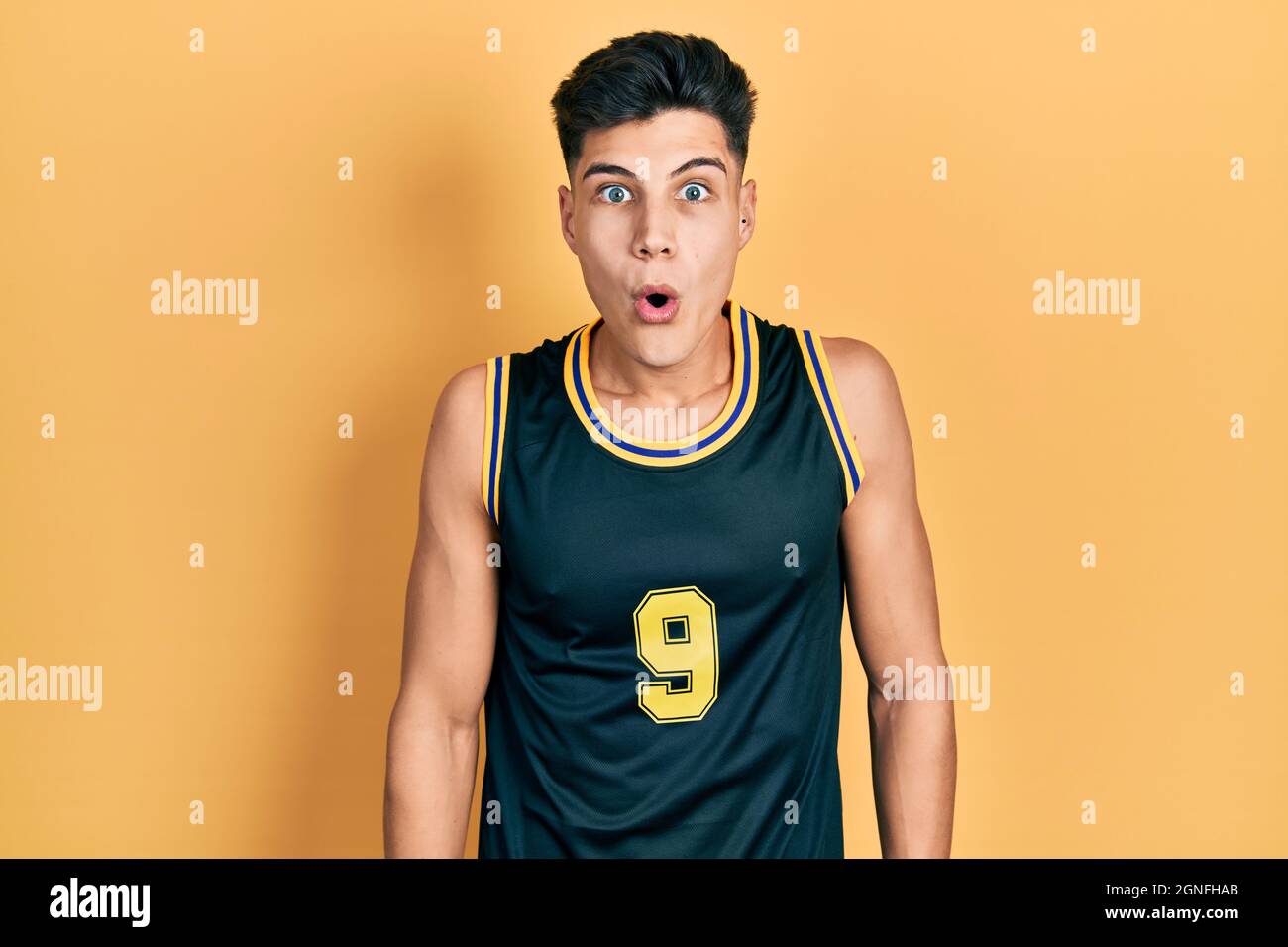 Young hispanic man wearing basketball uniform afraid and shocked with ...