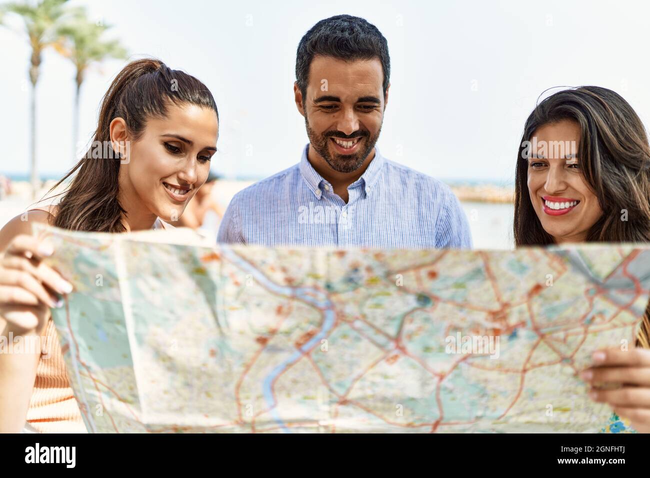 Three young hispanic friends smiling happy searching route on city map ...