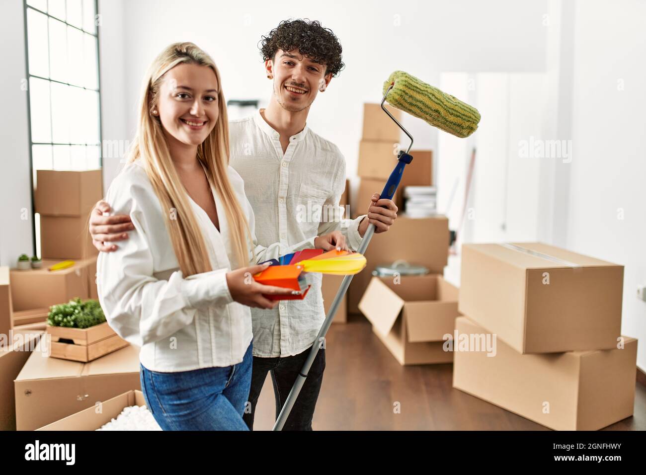 Young beautiful couple choosing paint color holding roller at new home ...