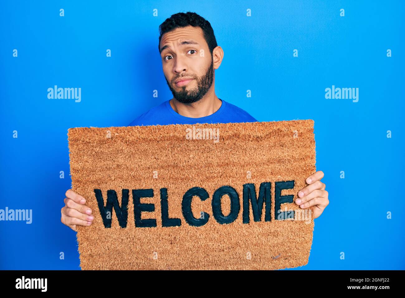 Hispanic man with beard holding welcome doormat clueless and confused ...