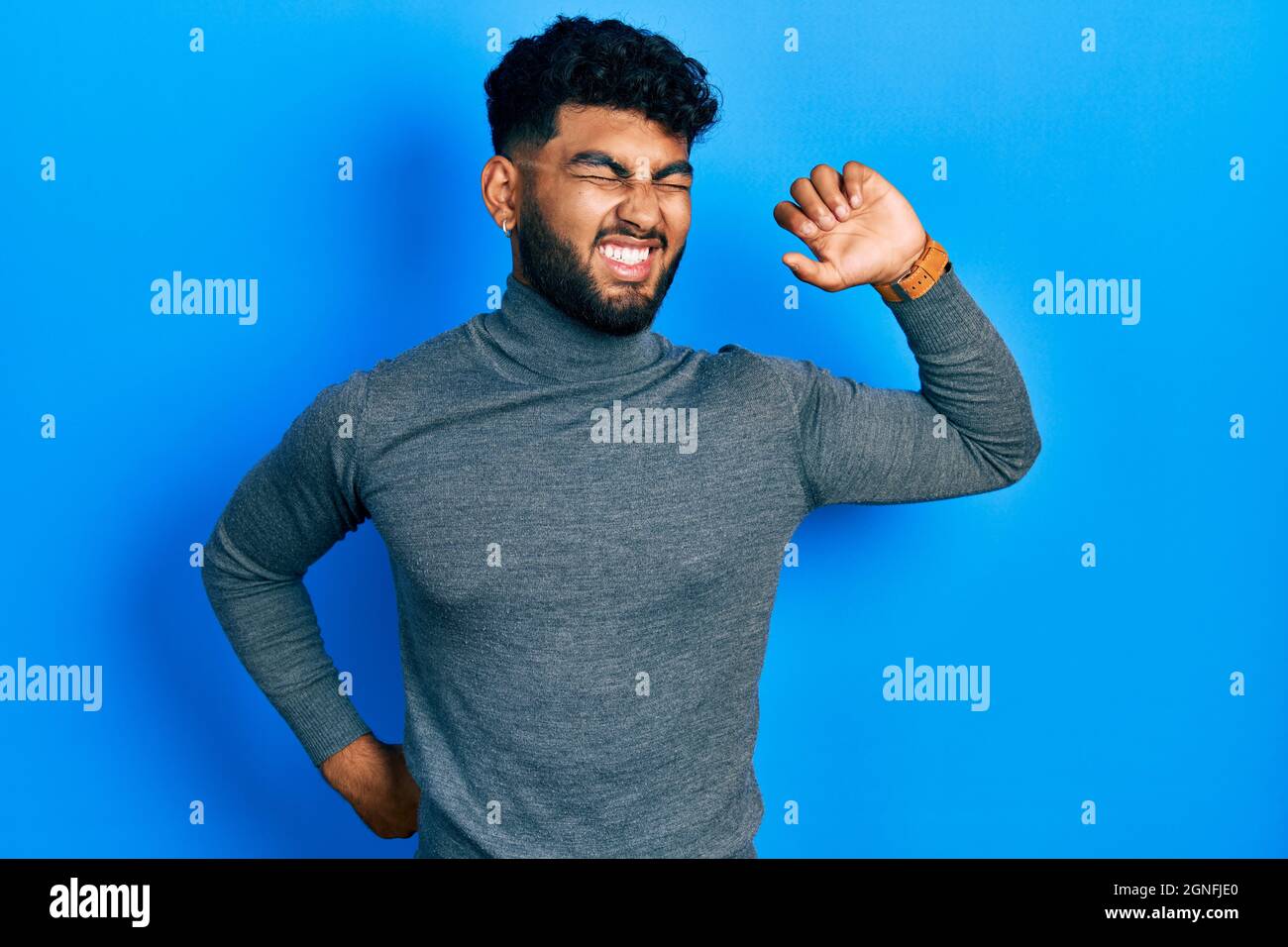 Arab man with beard wearing turtleneck sweater stretching back, tired ...