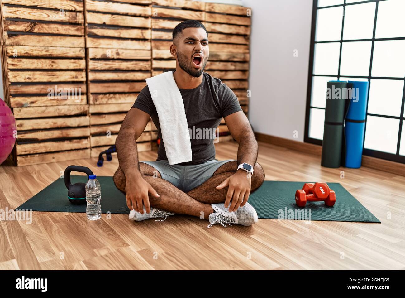 Young indian man sitting on training mat at the gym angry and mad ...