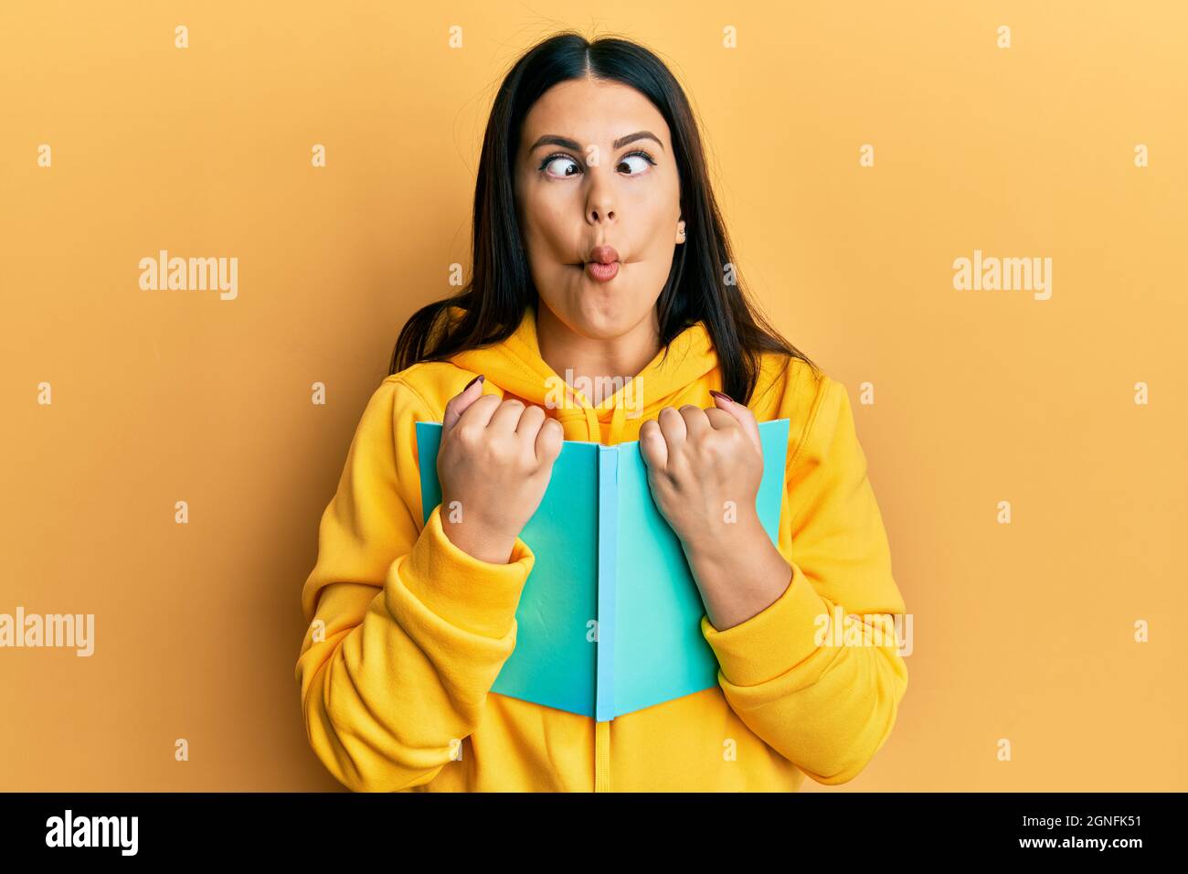 Beautiful brunette woman holding book making fish face with mouth and ...
